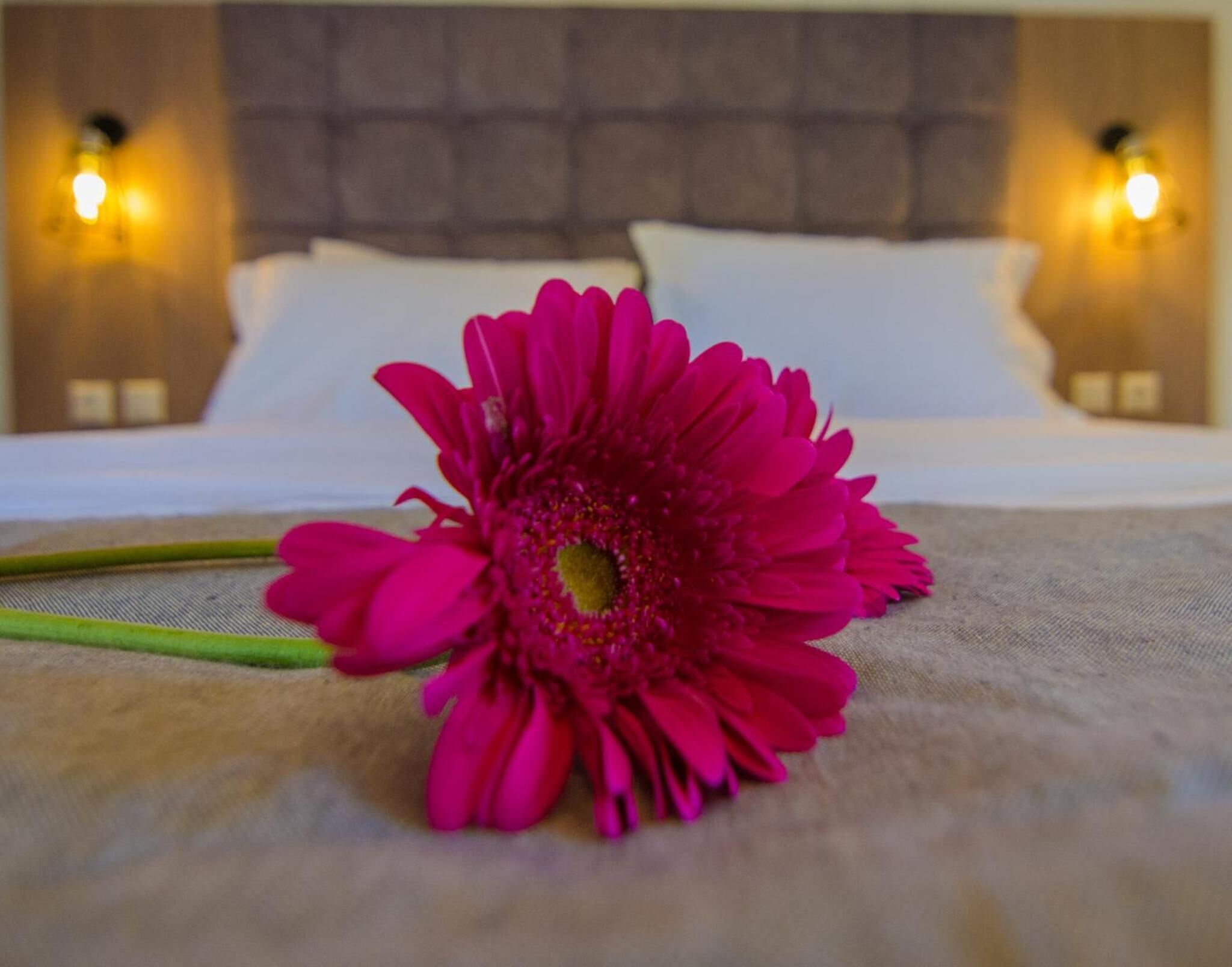 Uma cama com lençóis brancos e uma flor cor-de-rosa sobre o edredom.