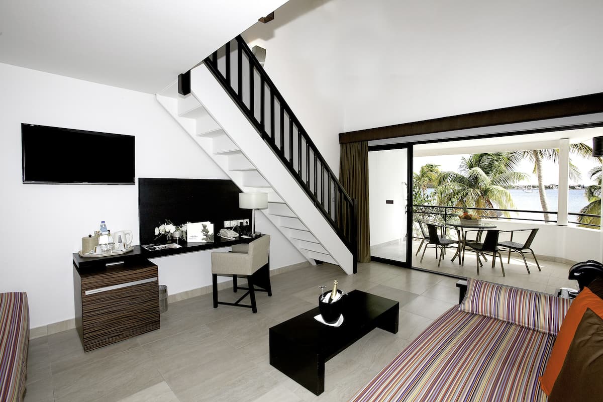 Uma sala de estar moderna com escada, área de jantar com vista e varanda com palmeiras.