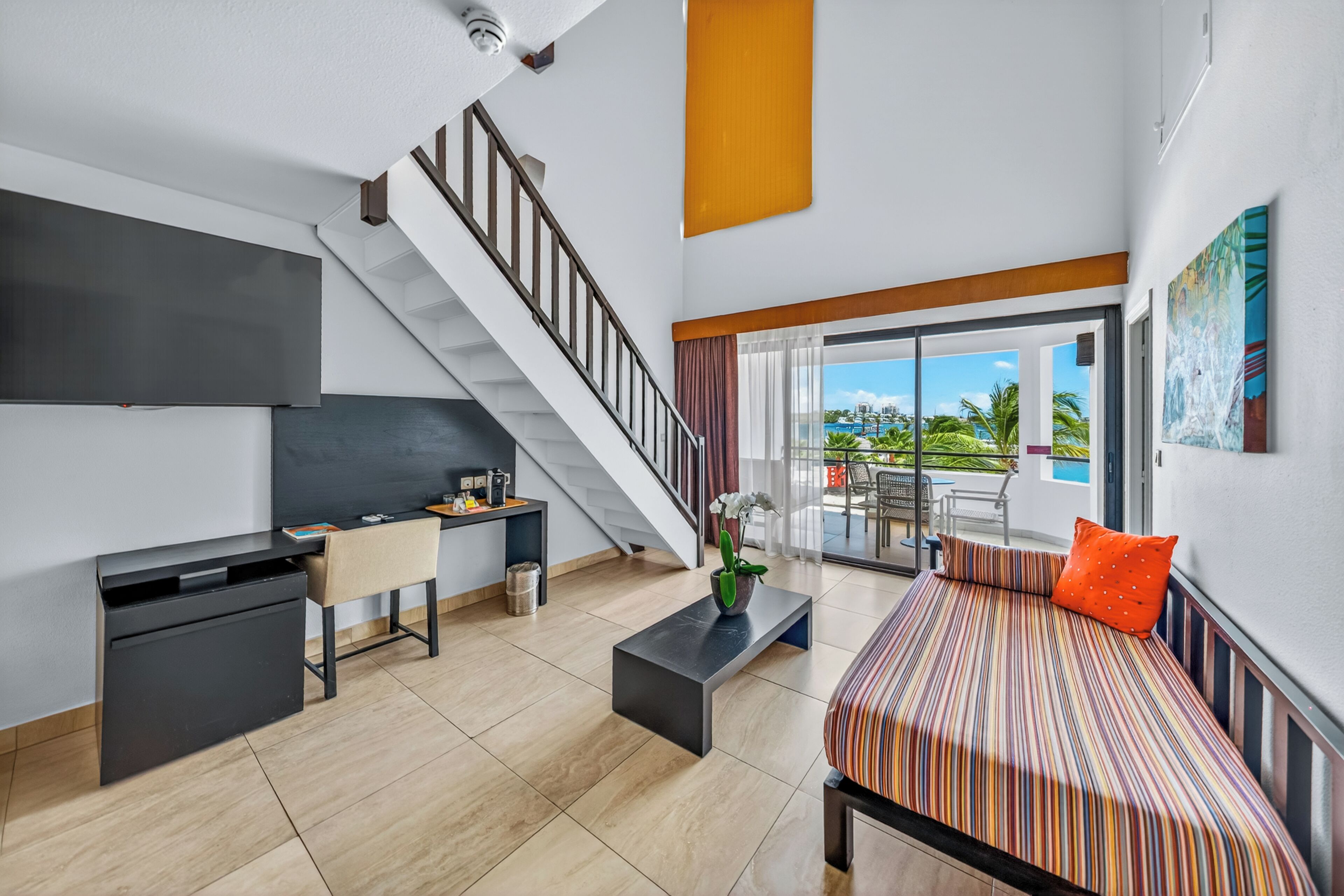 Uma sala de estar moderna com escada, uma mesa de escritório, uma cama e uma varanda com vista.