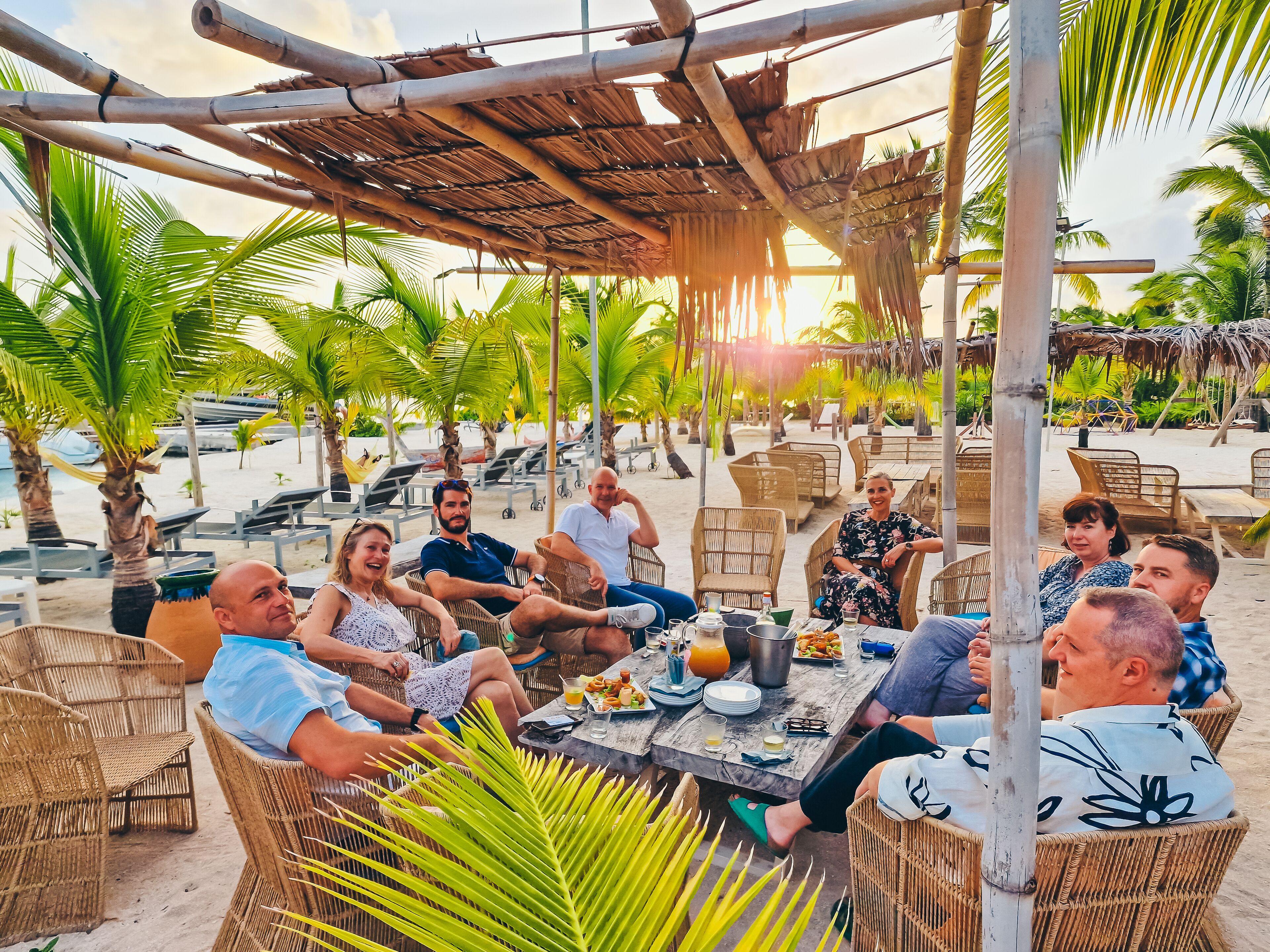 Um grupo de pessoas sentadas à mesa com vista para a praia e palmeiras.