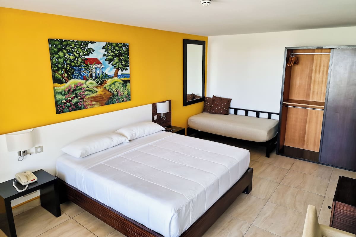 Quarto de hotel com cama, mesa de cabeceira, luminária e um quadro na parede.