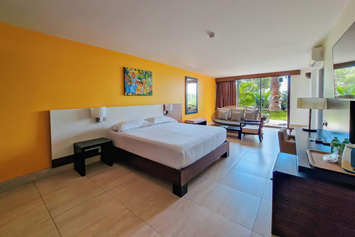 Quarto de hotel com cama, escrivaninha, cadeira, televisão e janela com vista para o verde.