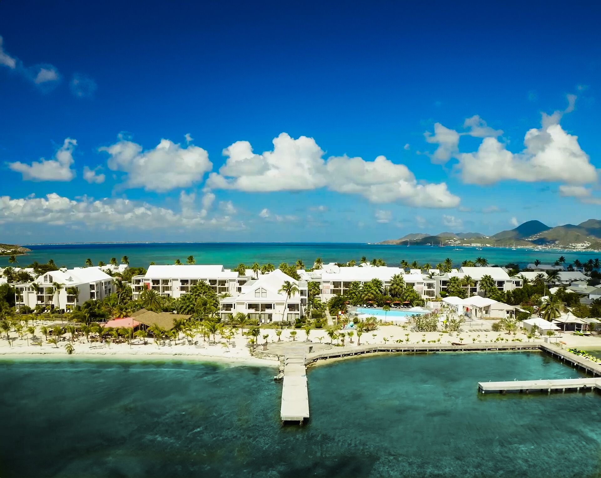 Um resort com vários edifícios brancos, céu azul claro, praia e área de piscina.
