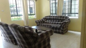 Uma sala de estar com um sofá estampado, uma mesinha de centro e uma janela com vista para o verde.