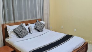 Cama bem arrumada com roupa de cama branca e almofadas estampadas com padrão de zebra, cabeceira de madeira e mesa de cabeceira.