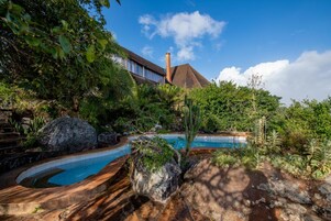 Uma piscina rodeada por rochas e vegetação exuberante, com um edifício ao fundo.