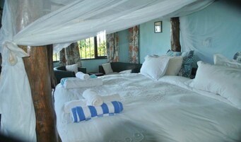 Quarto com cama, almofadas, uma cadeira e uma janela.