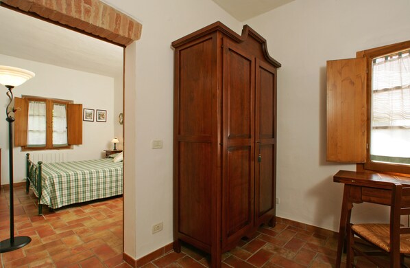 Quarto com cama, guarda-roupa de madeira, escrivaninha e janela com cortinas.