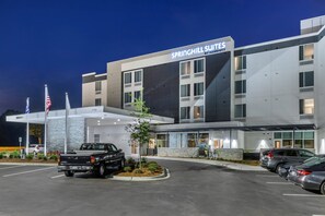 Um hotel moderno com uma placa indicando "Springhill Suites by Marriott". Vários carros estão estacionados na frente, e o edifício tem um telhado plano e janelas grandes.