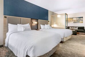 Quarto de hotel com duas camas grandes, um sofá e uma divisória de vidro.