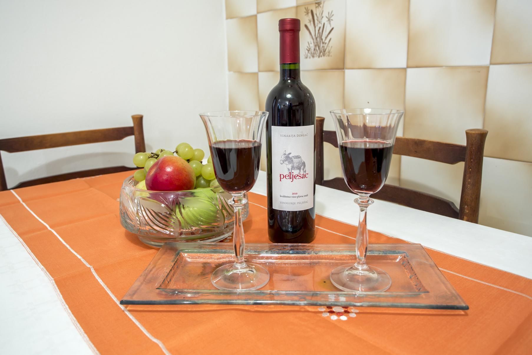 Uma mesa com uma garrafa de vinho, duas taças de vinho e uma cesta de frutas.