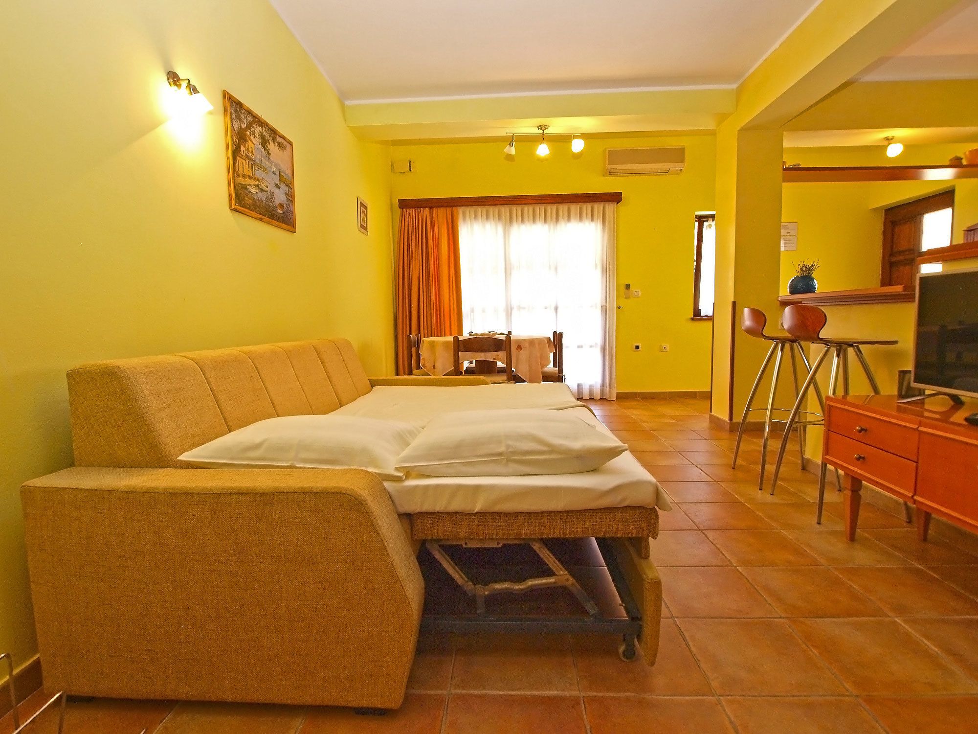 Quarto de hotel com sofá-cama, televisão, mesa pequena e uma cadeira.