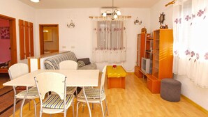 Uma sala de estar com uma mesa de jantar, cadeiras, um sofá, uma televisão e uma estante de livros.