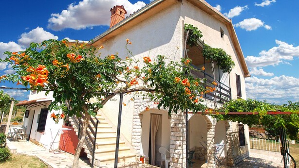 Uma casa rústica com um arco de pedra, escadaria de madeira e um jardim cheio de flores de laranjeira.