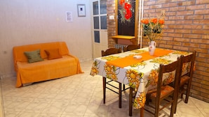 Uma área de refeições com uma mesa coberta por uma toalha de mesa com estampas de girassóis, rodeada por cadeiras de madeira.