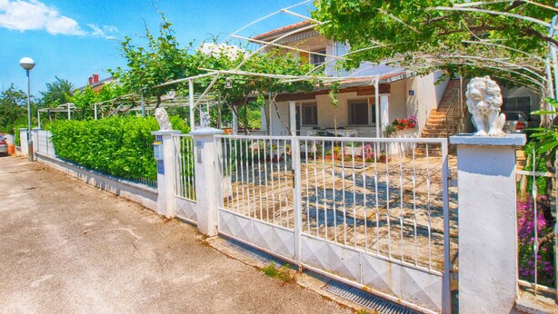 Um imóvel residencial com portão fechado, área de varanda coberta e escadaria que leva ao segundo andar.
