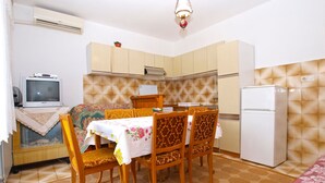Uma cozinha compacta com mesa de jantar, cadeiras, geladeira, fogão e uma televisão em um armário.