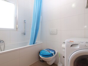 Casa de banho com banheira, sanita e máquina de lavar roupa.