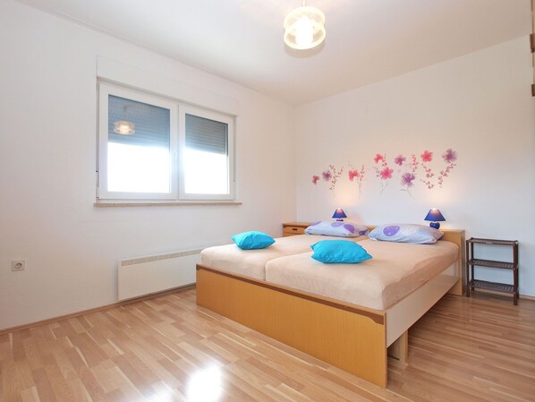 Quarto com cama de madeira, duas mesas de cabeceira com abajures, janela com persianas e parede com decoração floral.