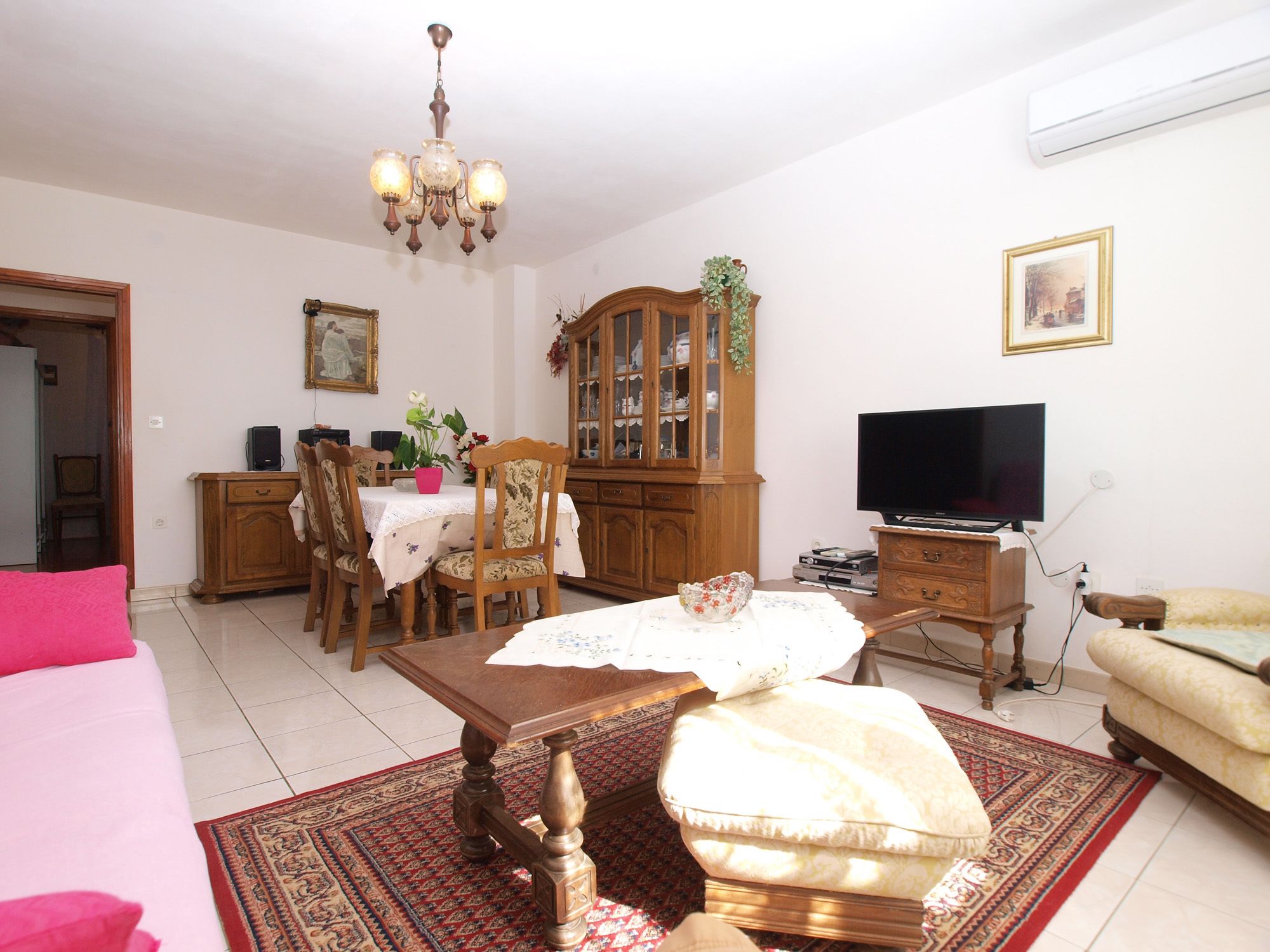 Uma sala de estar com uma mesa de jantar de madeira, cadeiras, um sofá, uma TV e um armário.