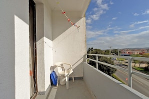 Varanda com parede branca, uma cadeira branca, um balde azul e uma cadeira de plástico branca.