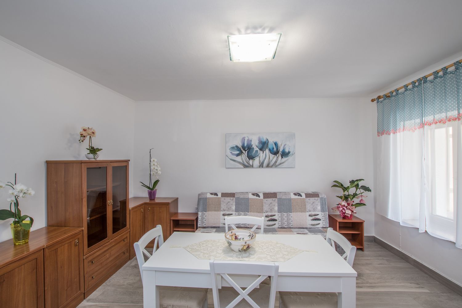 Uma sala de jantar com uma mesa branca, cadeiras, um armário de madeira e um sofá.