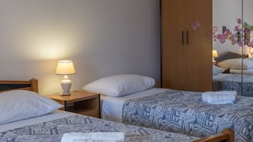 Quarto de hotel com duas camas, mesa de cabeceira com luminária, guarda-roupa e um espelho refletindo o quarto.