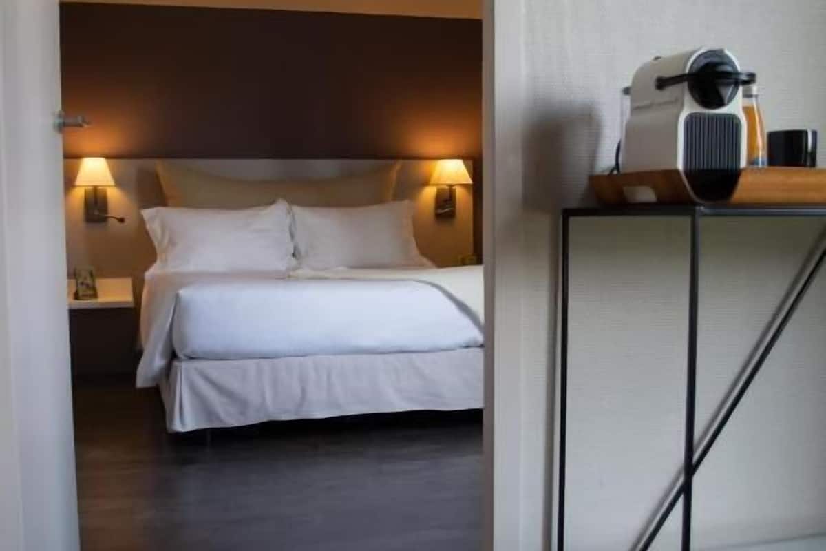 Quarto de hotel com cama, luminárias laterais, mesa de cabeceira e mesa com abajur.
