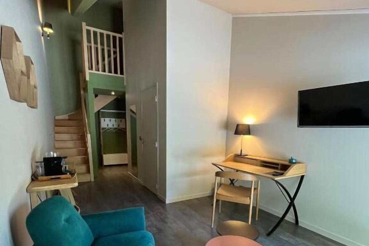 Uma sala de estar moderna com poltronas cor turquesa, uma mesa redonda pequena, uma TV e uma escada que leva a um mezanino.
