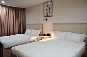 Quarto de hotel com duas camas, uma mesa de cabeceira com telefone e uma luminária na parede.