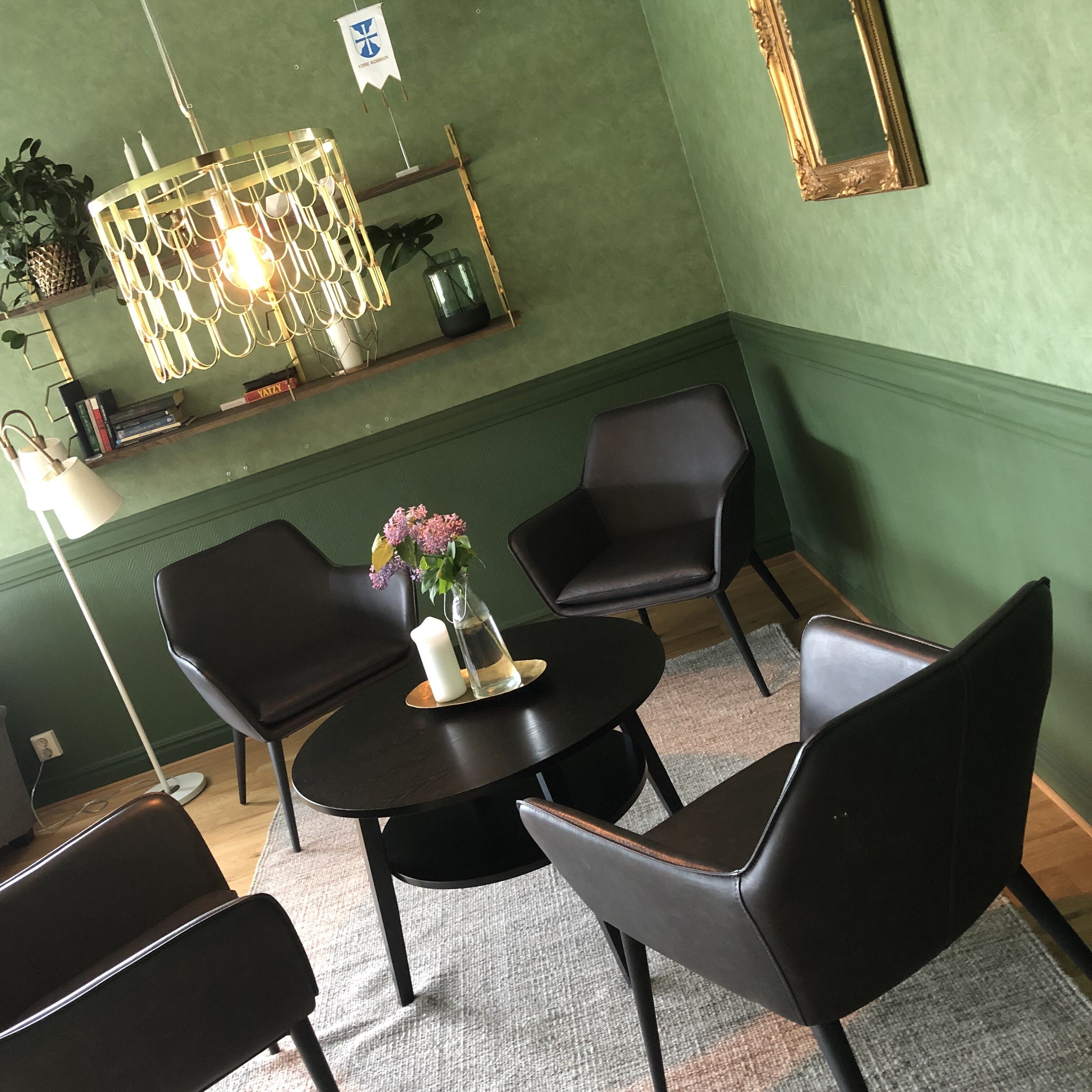 Quarto com uma mesa redonda, quatro cadeiras pretas, um vaso com flores, uma vela e um candeeiro decorativo.