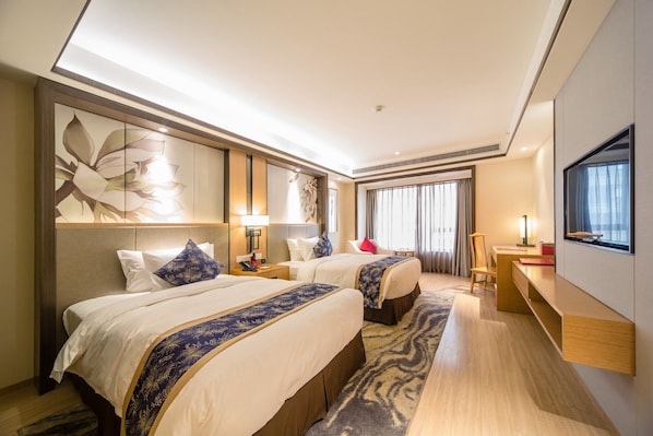 Quarto de hotel com duas camas, televisão, escrivaninha e uma janela grande com cortinas.