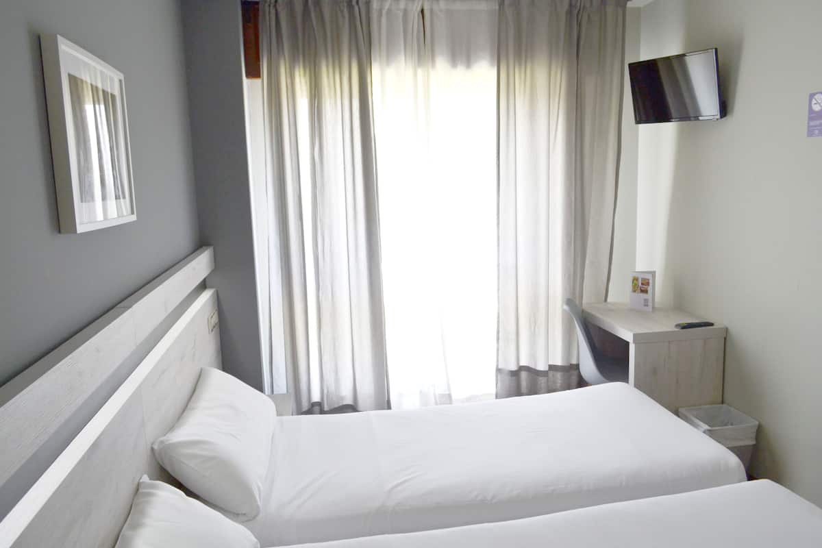 Quarto de hotel com duas camas, televisão fixada na parede e janela com cortinas.