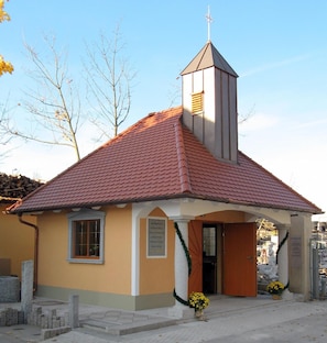 Uma pequena igreja com telhado de telhas vermelhas, um campanário e uma placa na frente.
