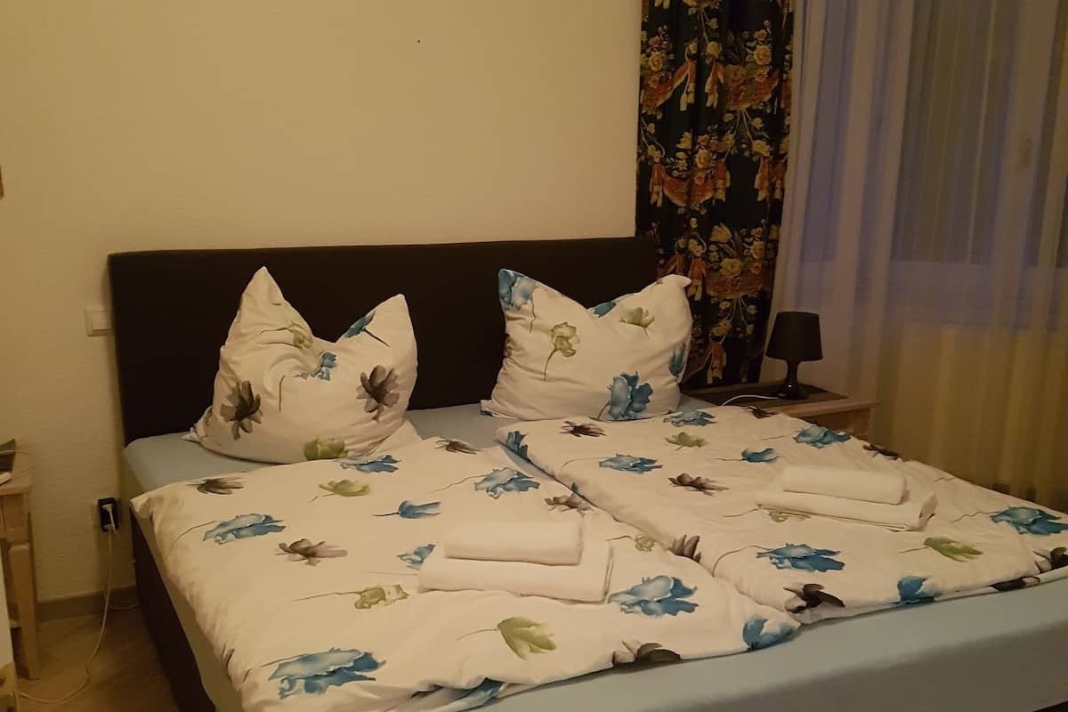 Cama bem arrumada com roupa de cama florida, cabeceira escura e abajur em uma mesa de cabeceira.