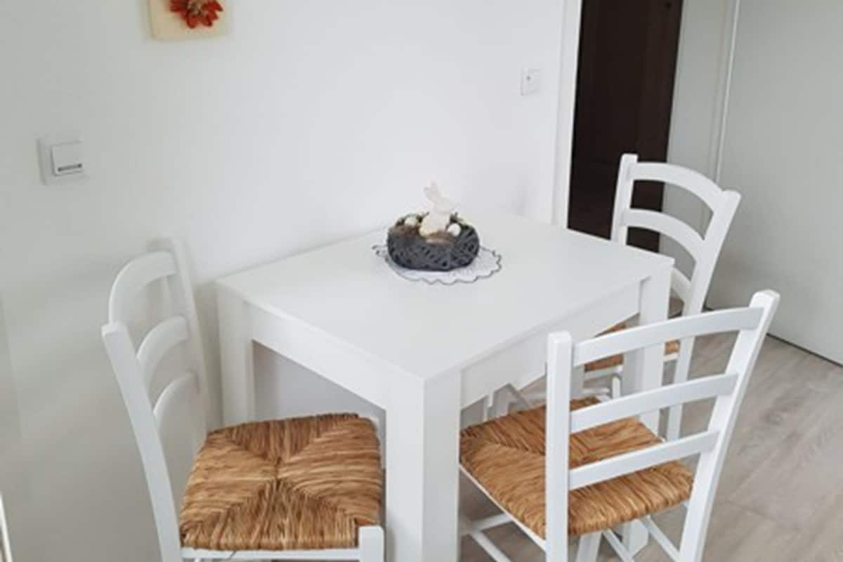 Mesa de jantar branca com quatro cadeiras, um relógio de parede e um letreiro escrito 'HOME'.