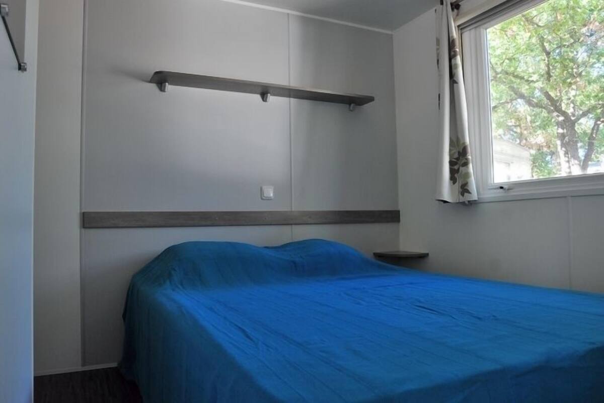 Quarto com uma cama, um estante e uma janela com cortinas.