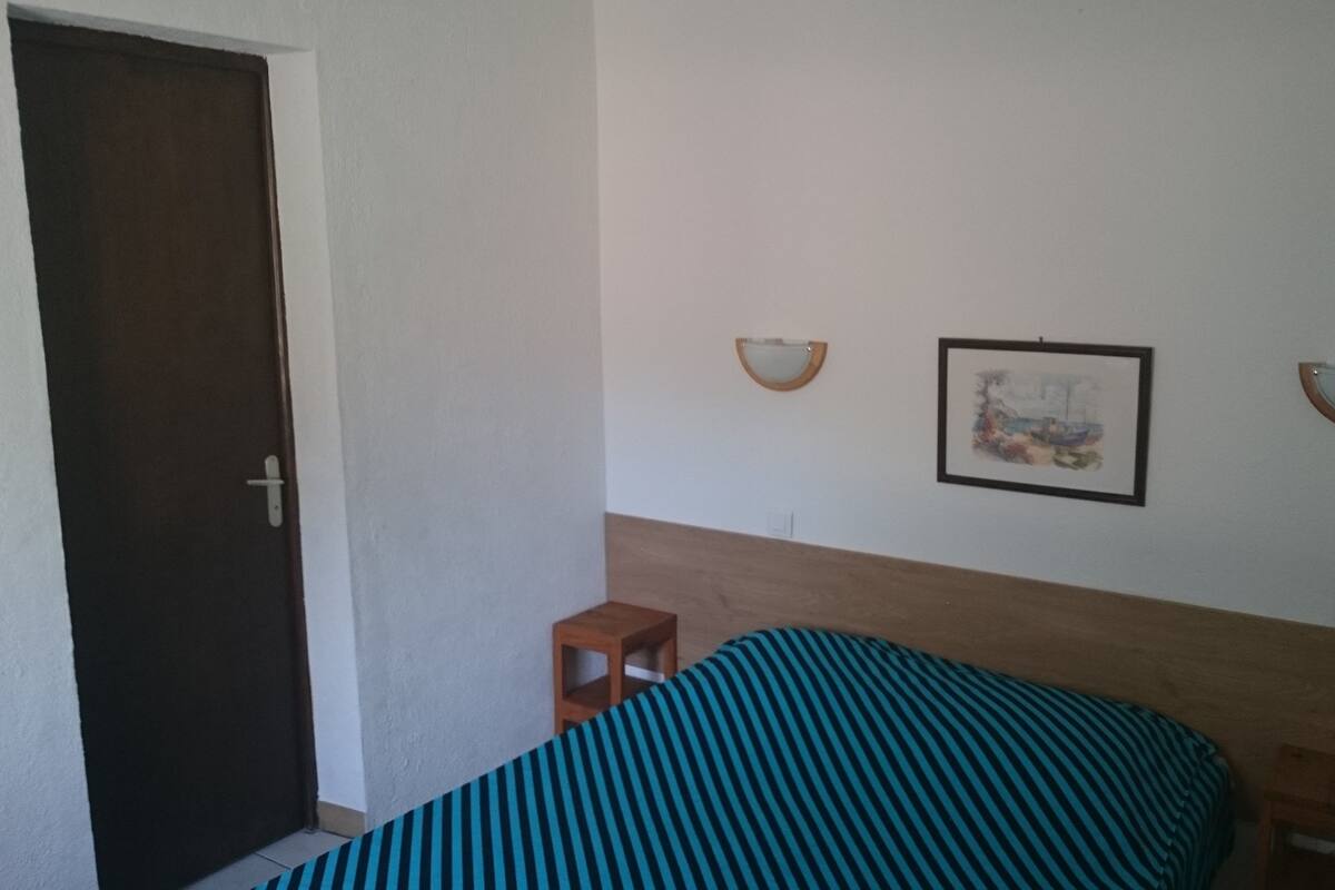 Quarto com cama, cabeceira de madeira, um pequeno banco de madeira e dois espelhos fixados na parede.