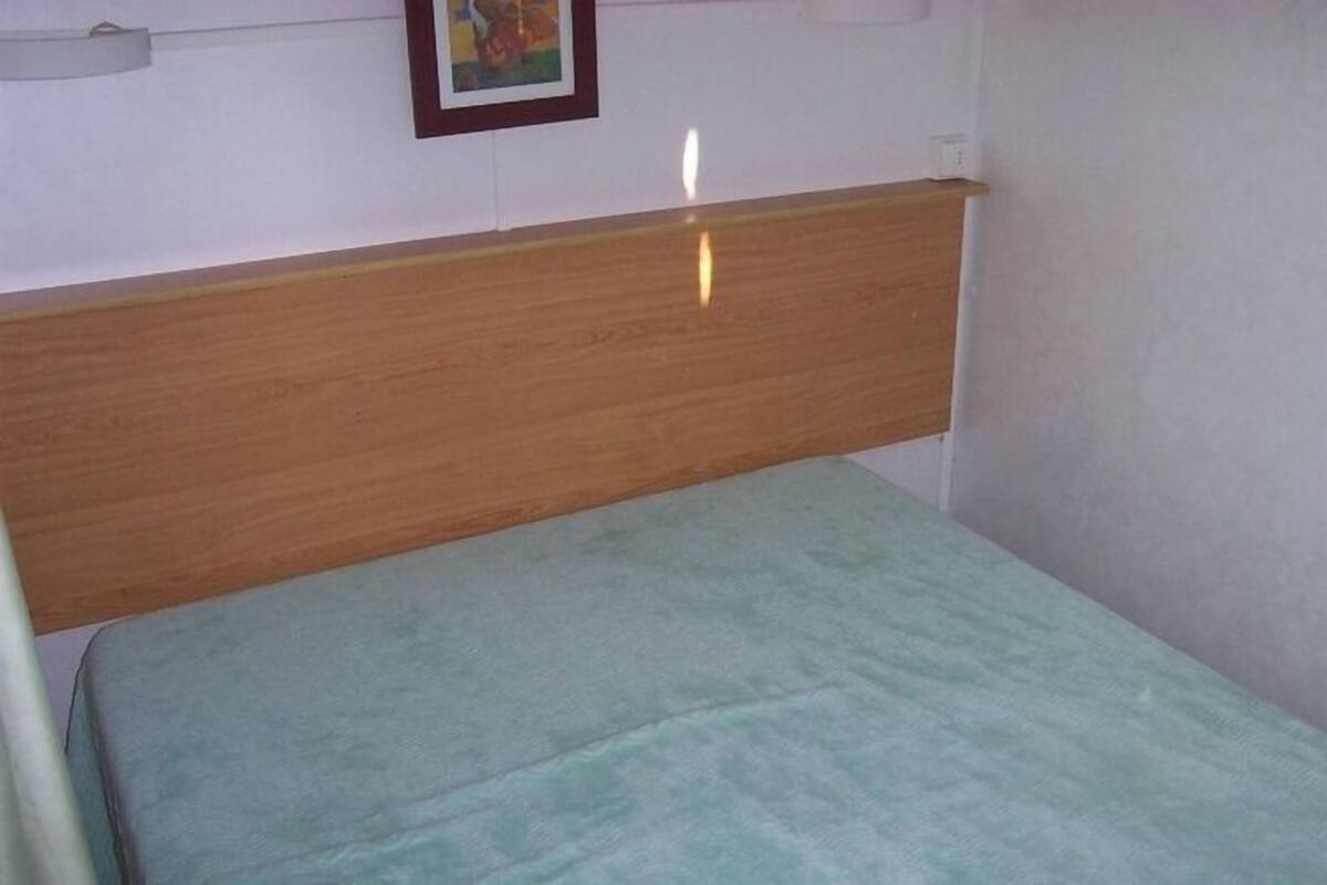Quarto pequeno com uma cama de solteiro, cabeceira de madeira e colcha verde claro.