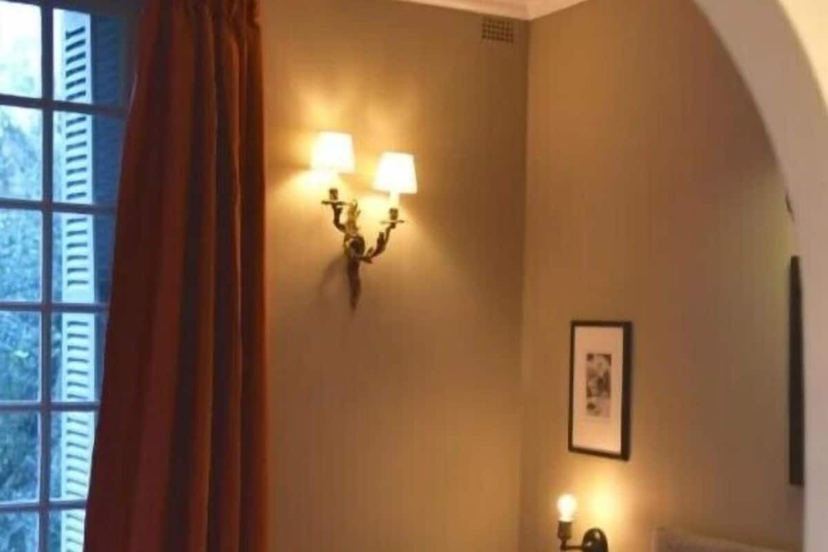 Quarto de hotel com uma cama, janela com cortinas, luminária fixada na parede e um quadro emoldurado.