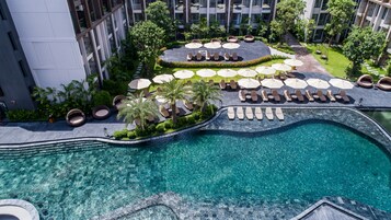 Área de piscina no terraço com espreguiçadeiras e guarda-sóis, rodeada por vegetação e edifícios modernos.