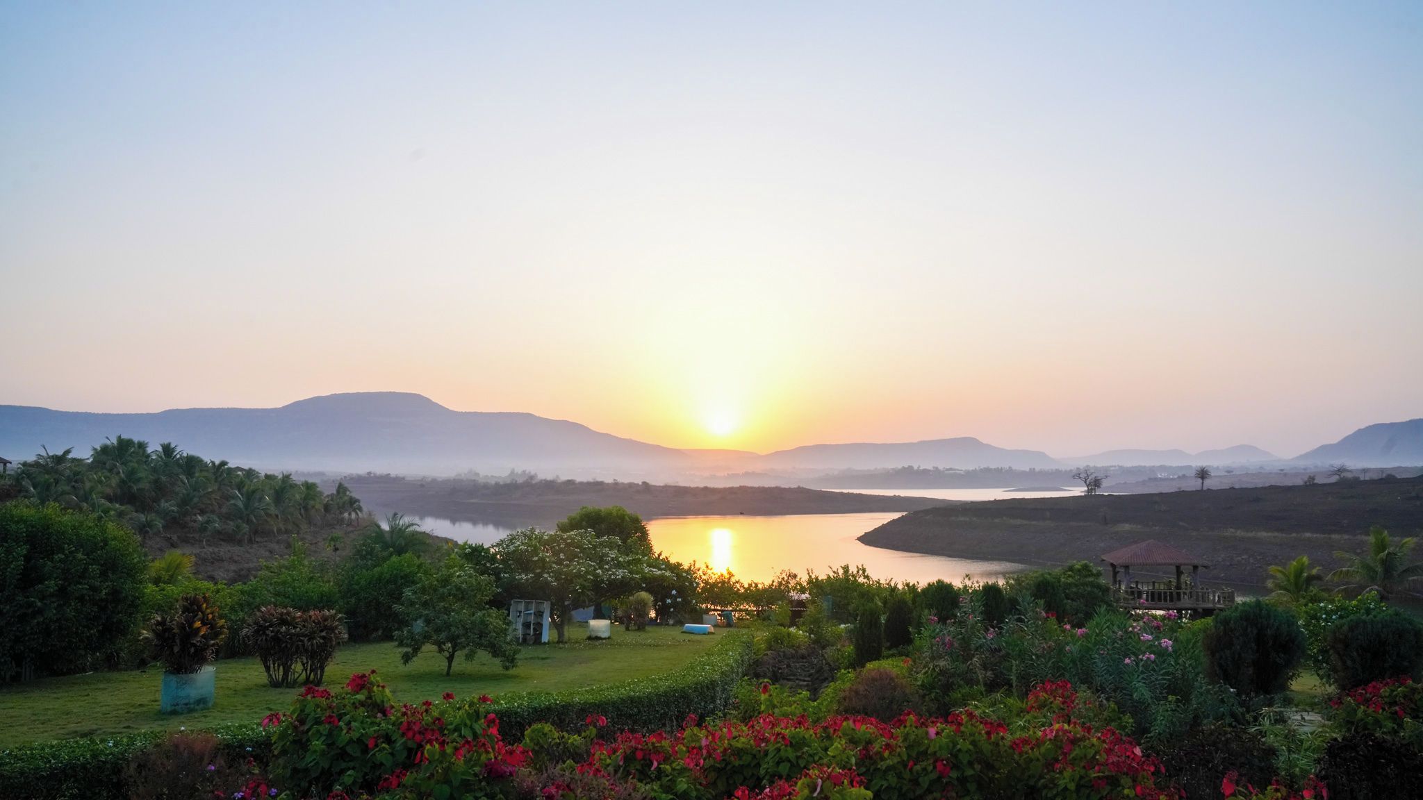 Paisagem tranquila com um corpo d'água, vegetação e colinas ao longe durante o pôr do sol.