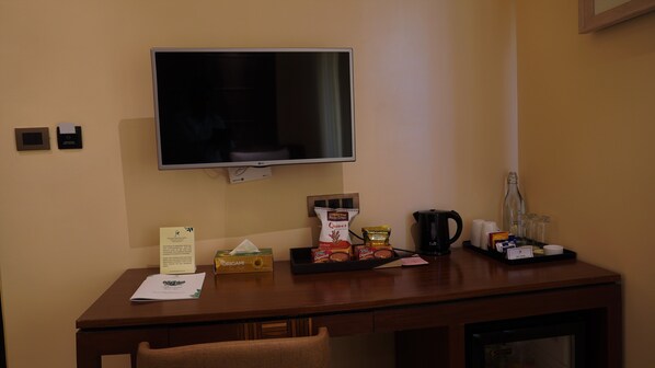 Mesa de quarto de hotel com televisão, máquina de café, lanches e caixa de lenços.