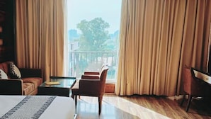 Quarto de hotel com cama, sofá, poltrona, mesa pequena e vista para o exterior.