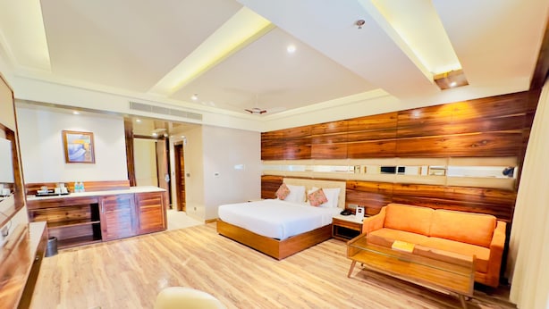 Quarto de hotel moderno com piso de madeira, uma cama grande, um sofá, uma escrivaninha e uma cadeira.
