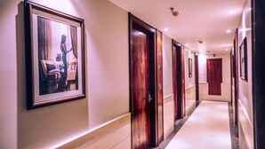 Um corredor com obras de arte emolduradas nas paredes, portas de madeira e chão de mármore.