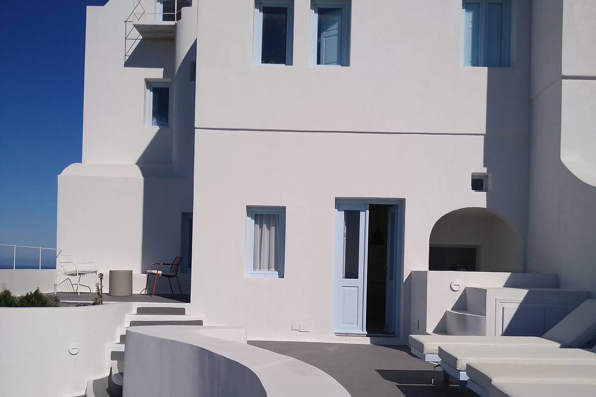 Um edifício moderno e branco com uma escadaria curva que leva a uma área externa coberta com espreguiçadeiras.