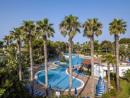 Um resort com uma grande piscina rodeada por palmeiras e espreguiçadeiras azuis.