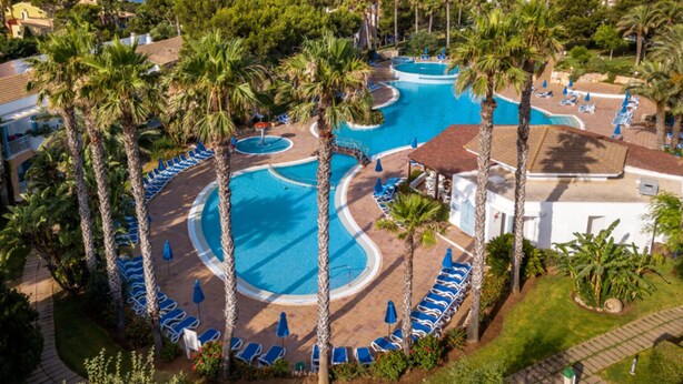Um resort com várias piscinas rodeadas por palmeiras, espreguiçadeiras e vista para o oceano.