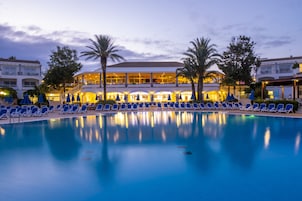 Um hotel com piscina, espreguiçadeiras e palmeiras.